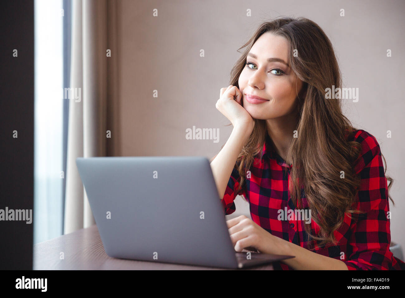 Portrait of a smiling pretty woman using laptop computer and looking at ...