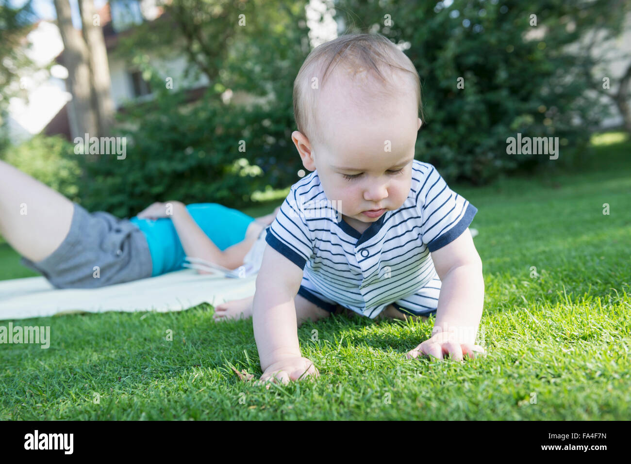 Baby boy exploring grass in lawn and his mother lying down in lawn ...