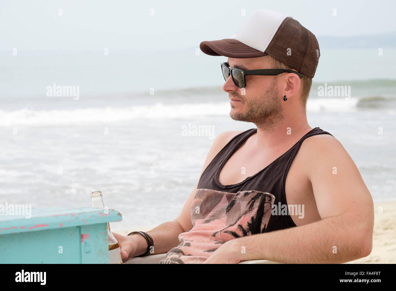 Young man enjoying a beer while sitting at the beach Stock Photo - Alamy