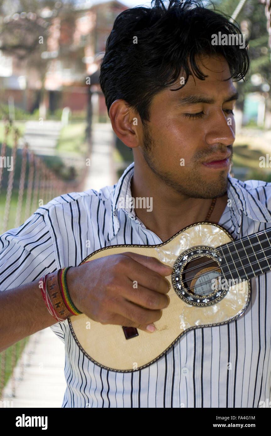Sunlit young man in striped shirt playing a charango, a traditional ...