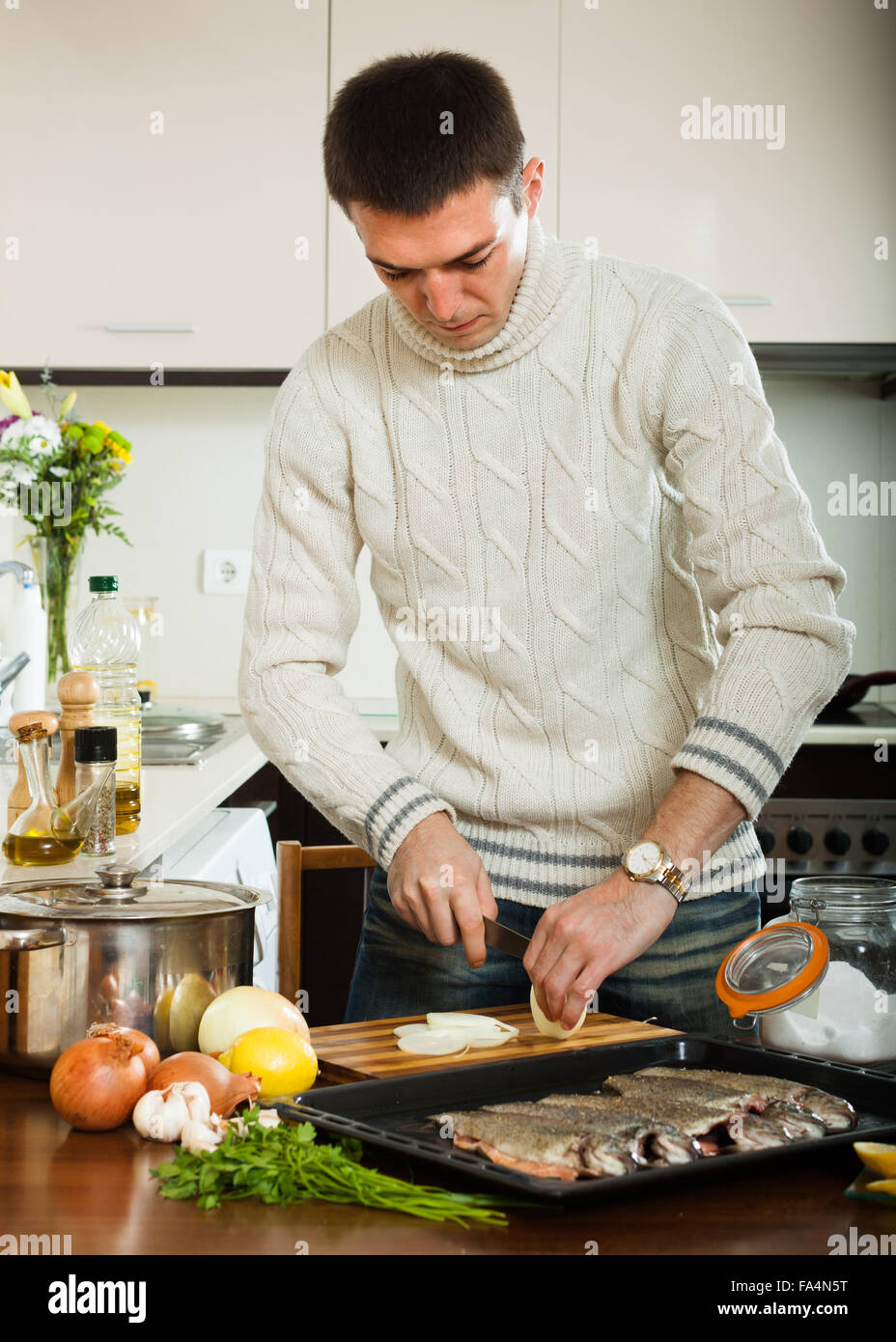 Handsome guy cooking raw fish with onion in roasting pan at kitchen ...