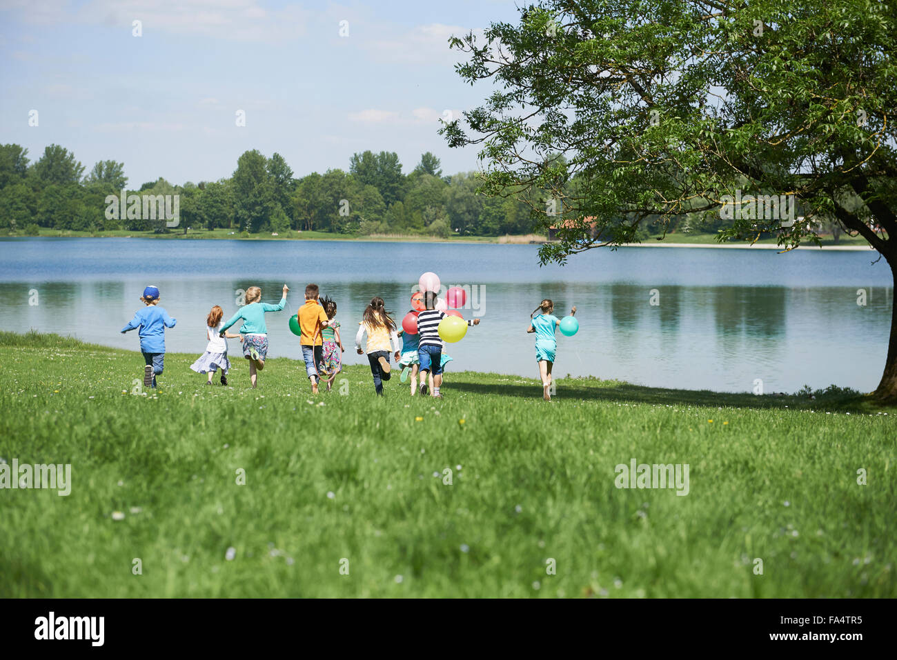 Rear view of children running in park with balloons, Lake Karlsfeld ...