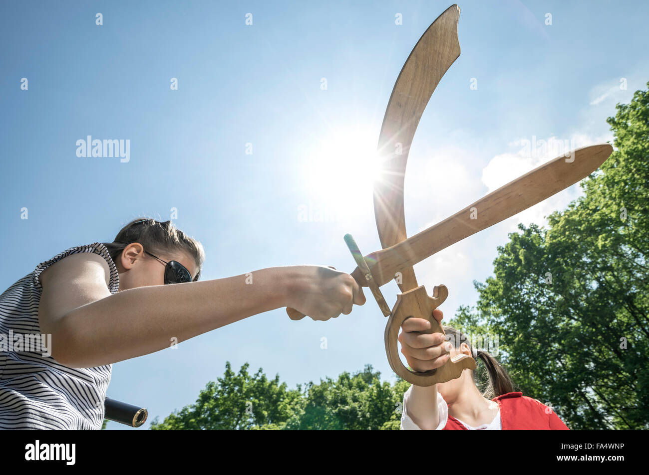 Low angle view of two girls pretending as pirates fighting with swords ...