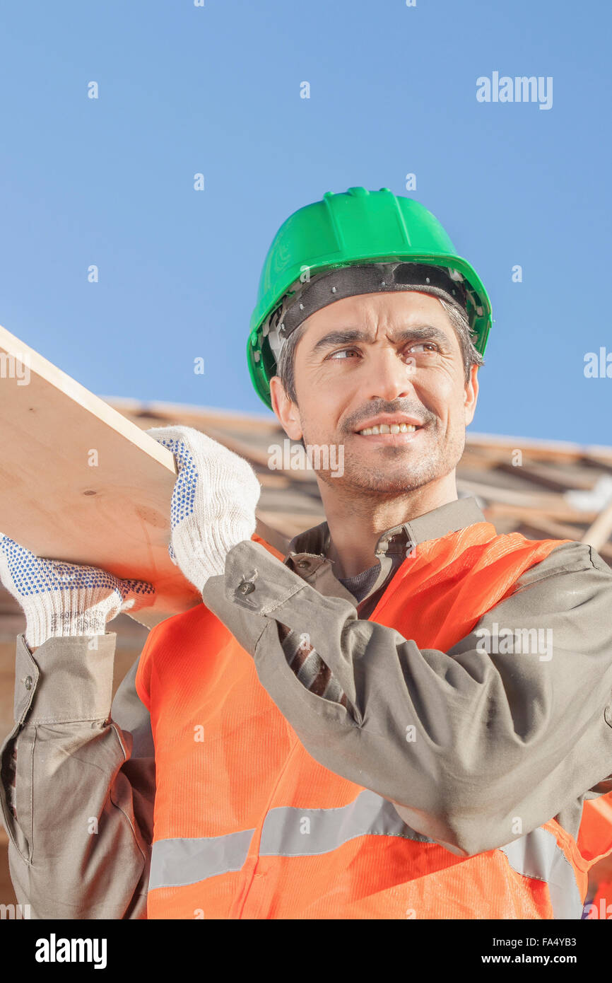 An orange vested laborer helping another carry a board Stock Photo - Alamy