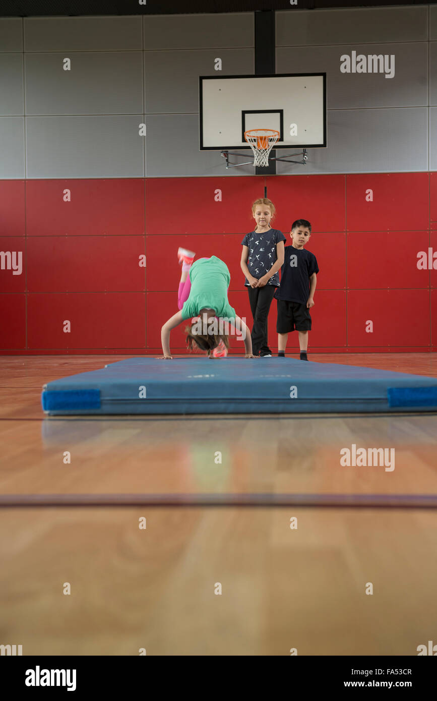 Girl doing somersault on exercise mat in sports hall with her friends ...