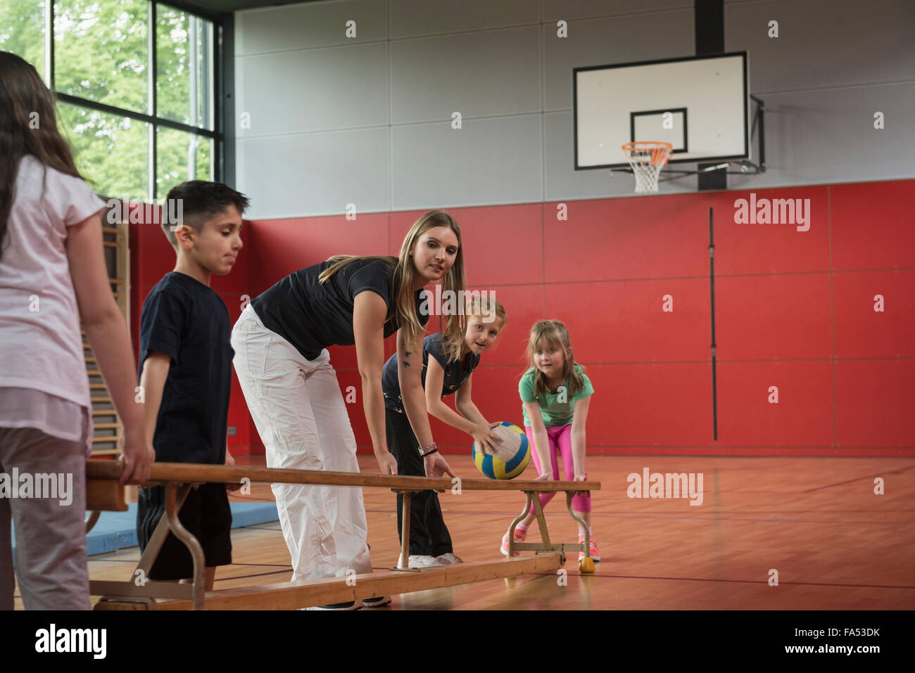 Teacher and students carrying bench in sports hall, Munich, Bavaria ...