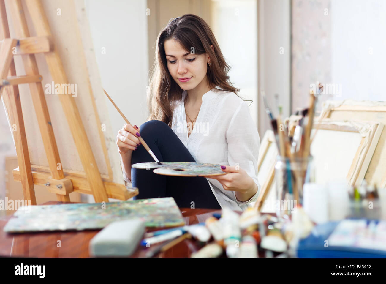 Long-haired beautiful artist paints on canvas in workshop Stock Photo ...