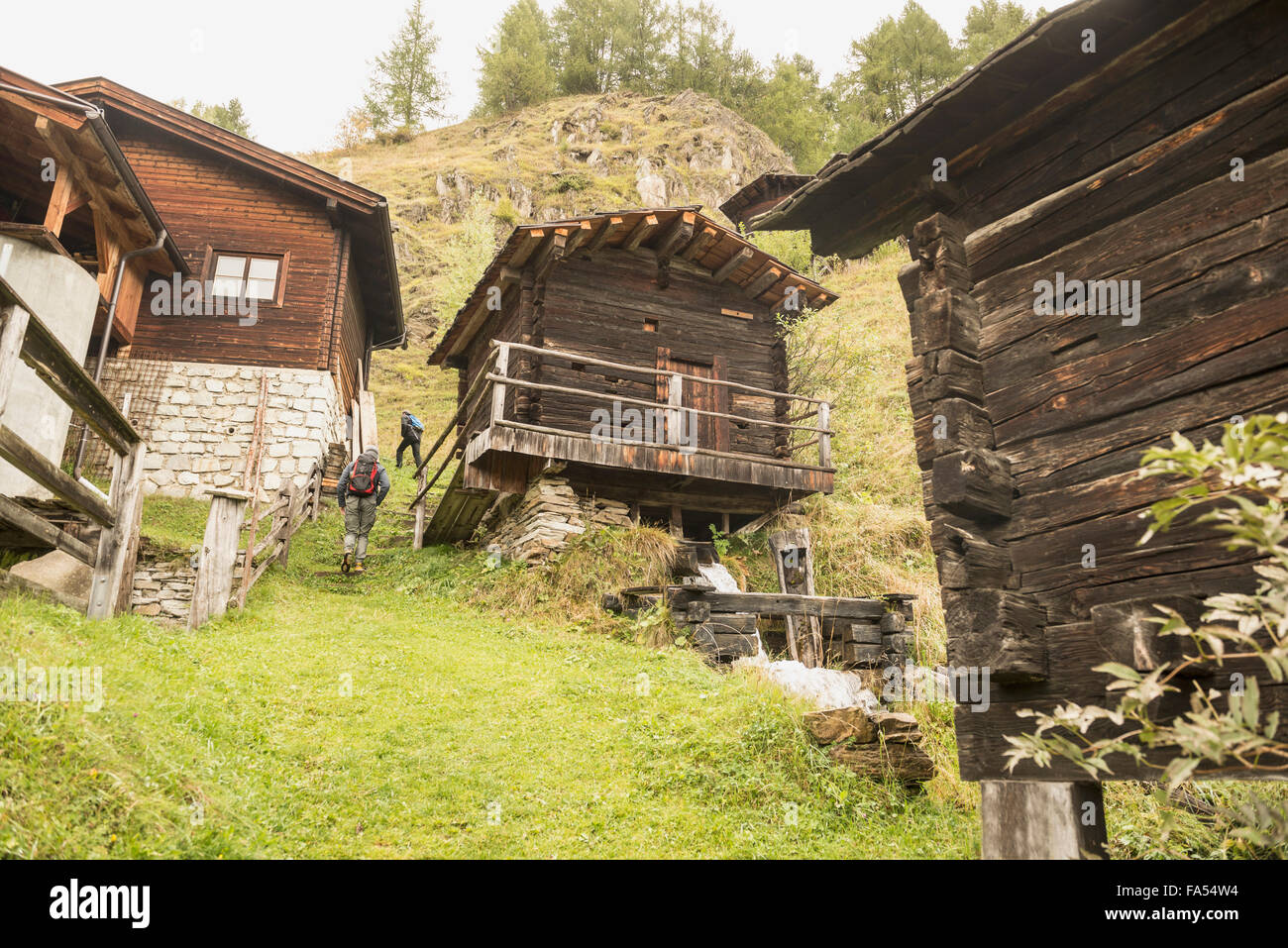 Rear view of two mature hikers passing by cottages, Austrian alps ...