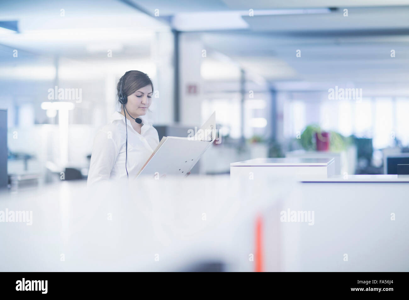 businesswoman wearing headset and reading document in cubicle, Freiburg ...