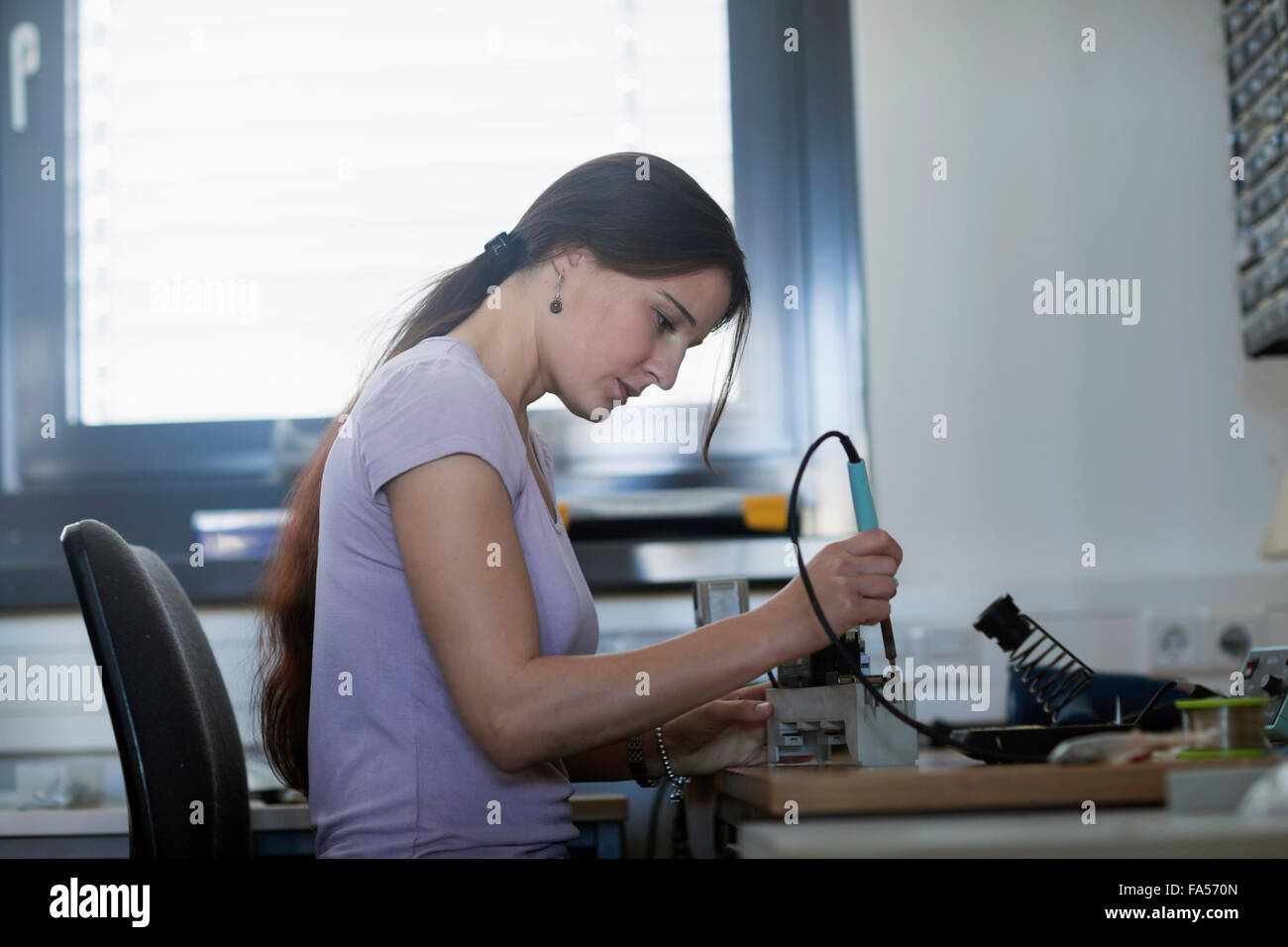 Female technician soldering electronic components in an industrial ...