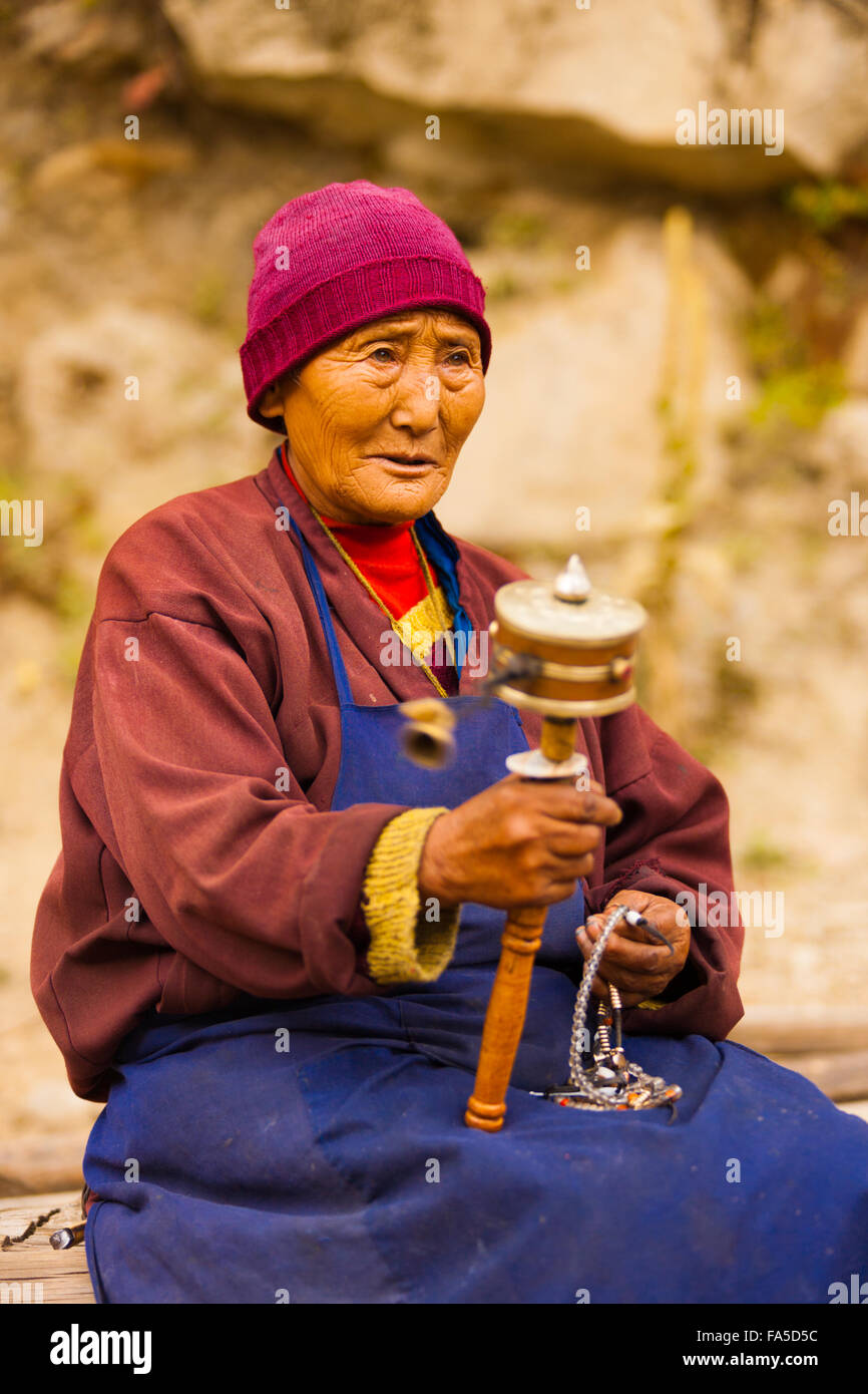 Female Tibetan pilgrim sitting in blue apron, holding beads and mani ...