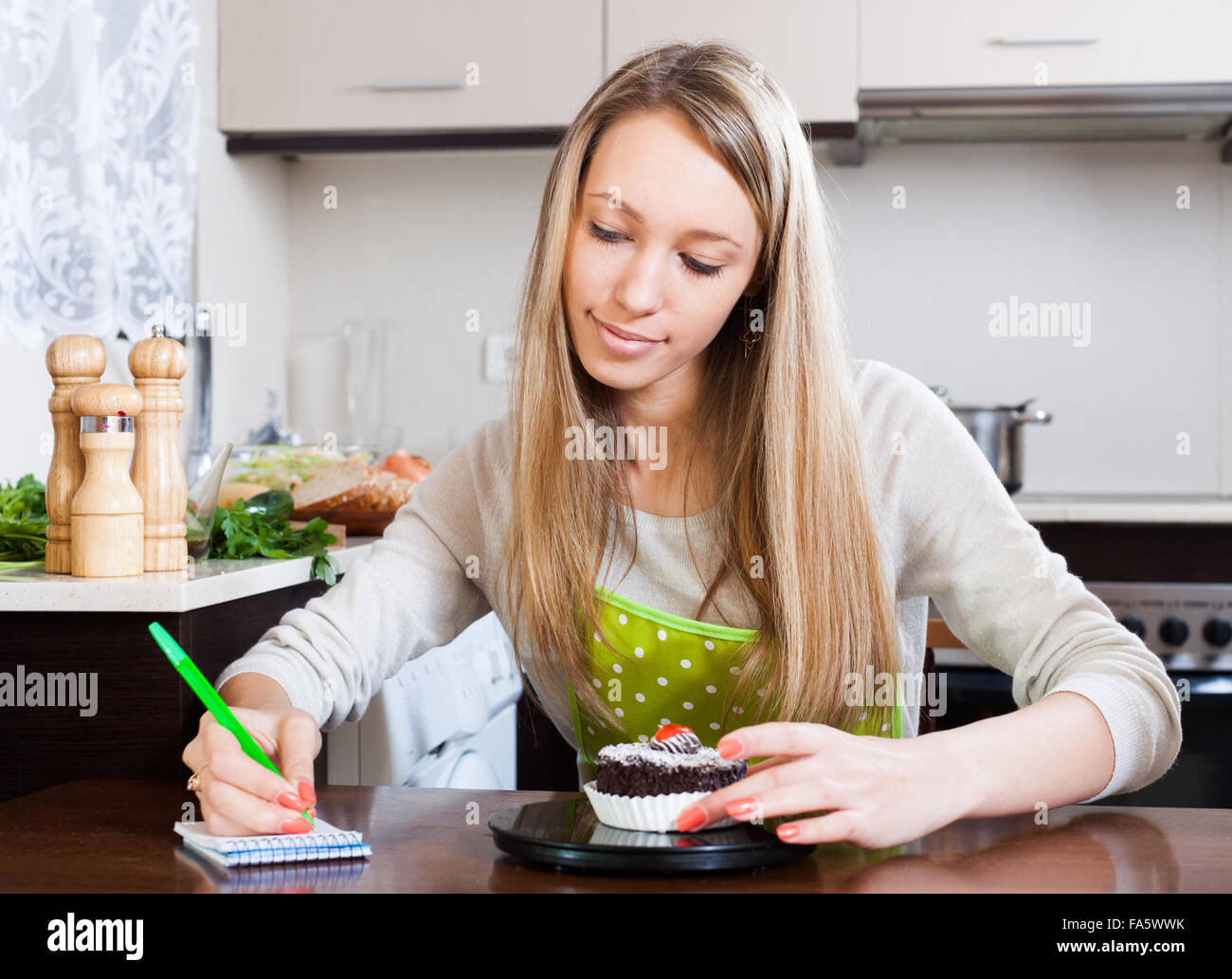 Smiling girl weighing cakes on kitchen scales at kitchen Stock Photo ...