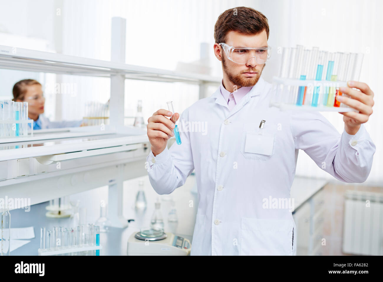 Young chemist looking at flasks with liquid chemical substances Stock ...