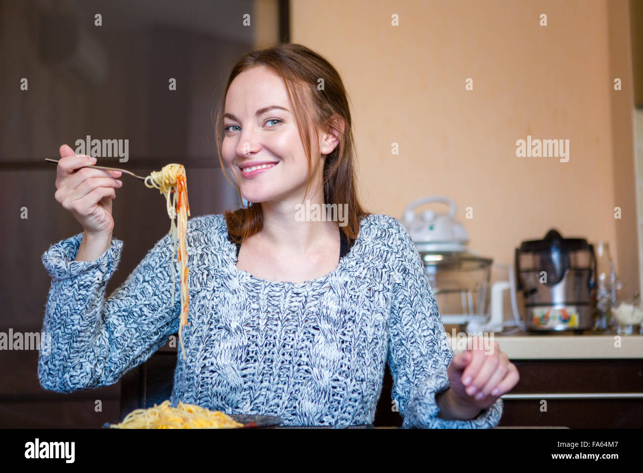 Beautiful cheerful young female in grey knitted sweater eating pasta in ...