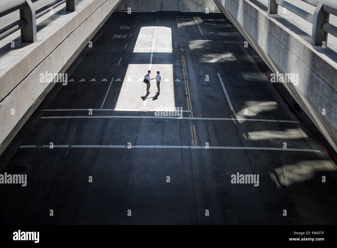 View from above onto a city plaza and two men walking from shadow into ...
