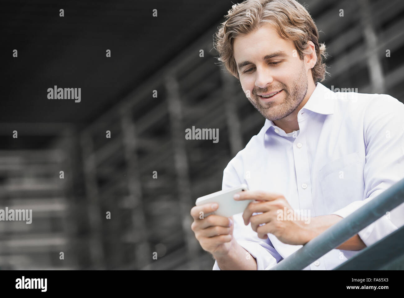 A man standing by a railing in a city, checking his smart phone Stock ...