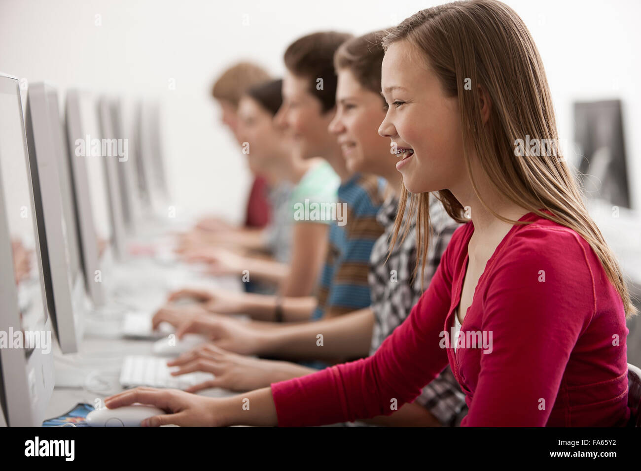 A group of young people, boys and girls, working at computer screens in ...