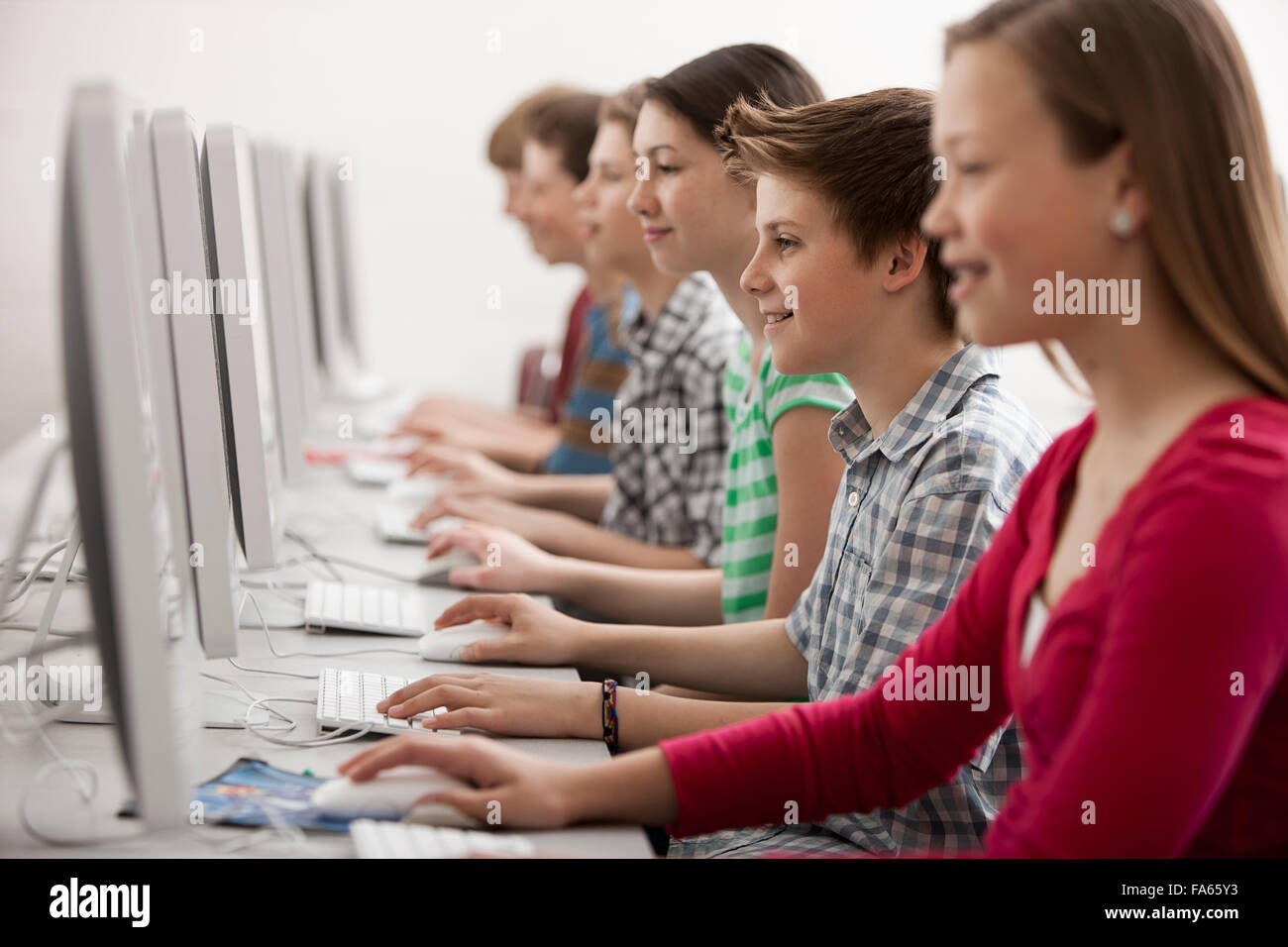 A group of young people, boys and girls, working at computer screens in ...