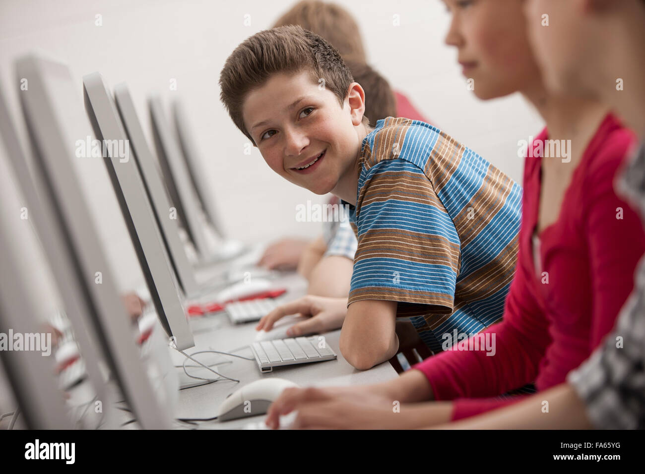 A group of young people, boys and girls, working at computer screens in ...