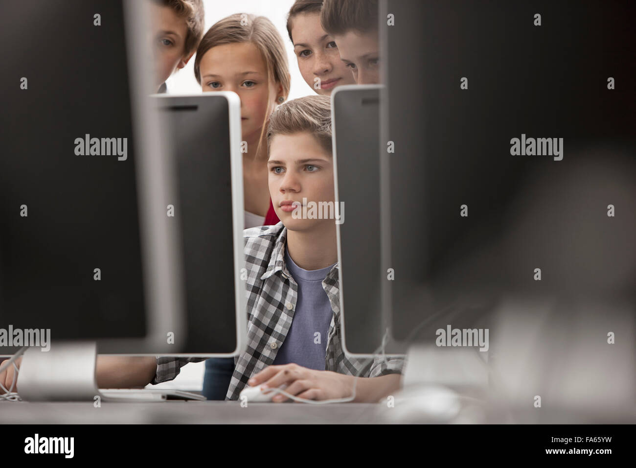A group of young people, boys and girls, working at computer screens in ...