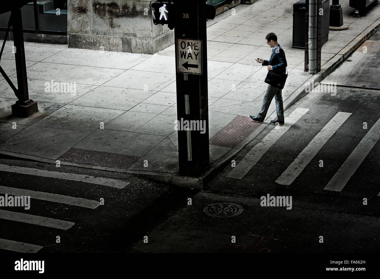 A man walking across a street crossing, looking at a phone in his hand ...