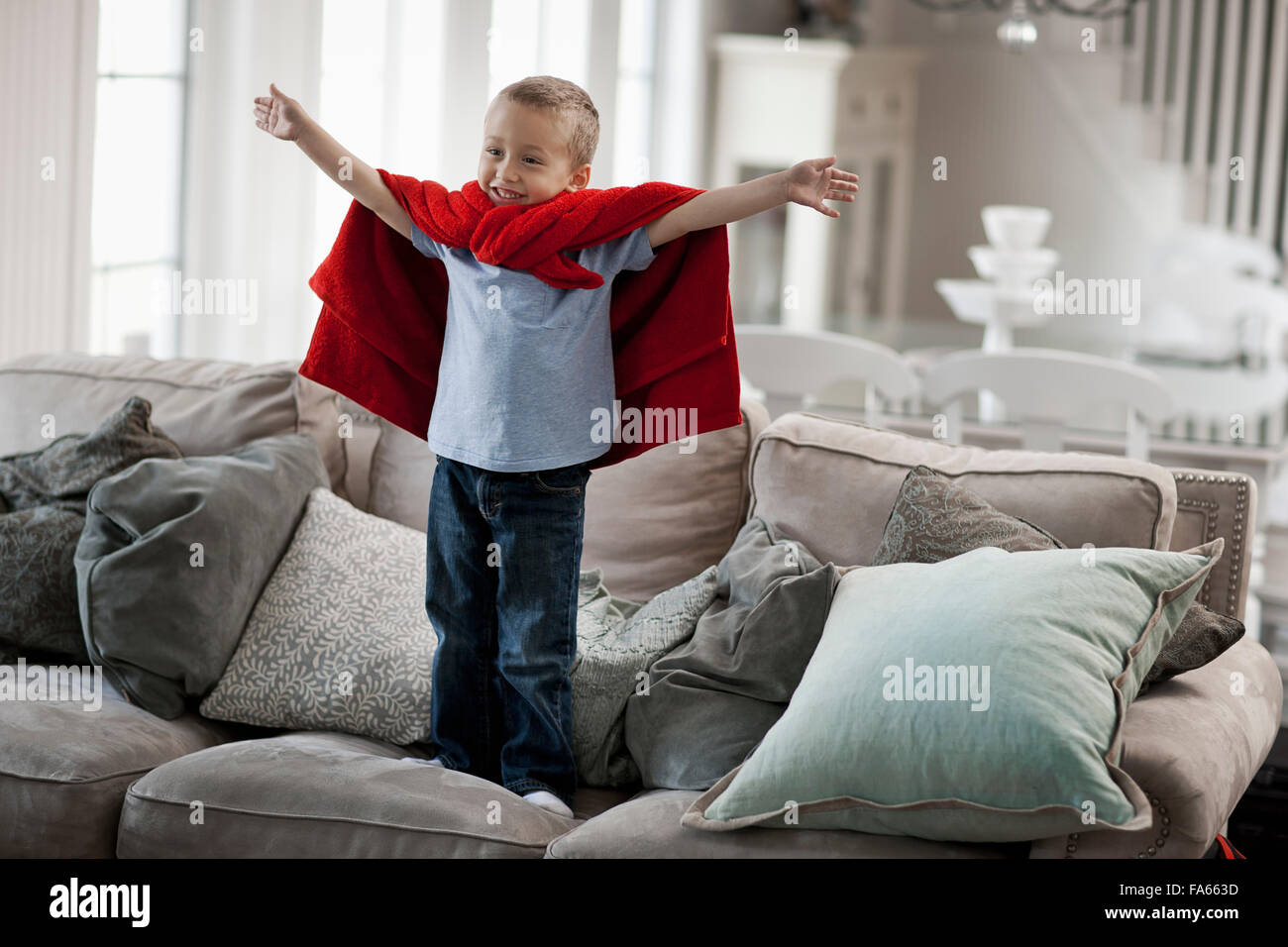 A child standing wearing a red cape, arms raised in a a superhero pose ...