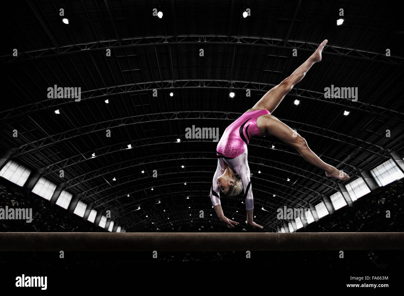 A young woman gymnast performing on the beam, balancing on her hands on ...