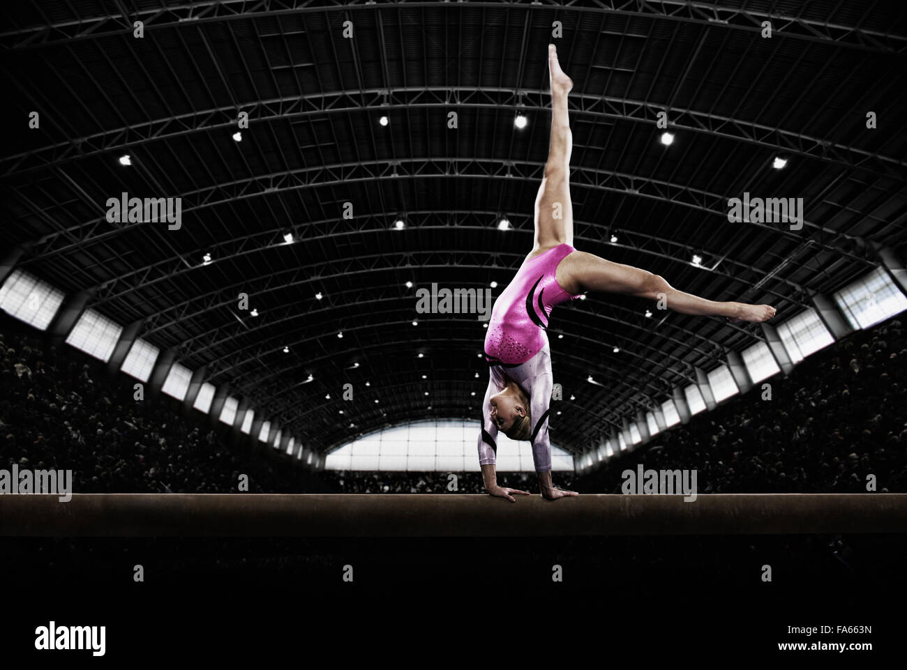 A young woman gymnast performing on the beam, balancing on her hands on ...