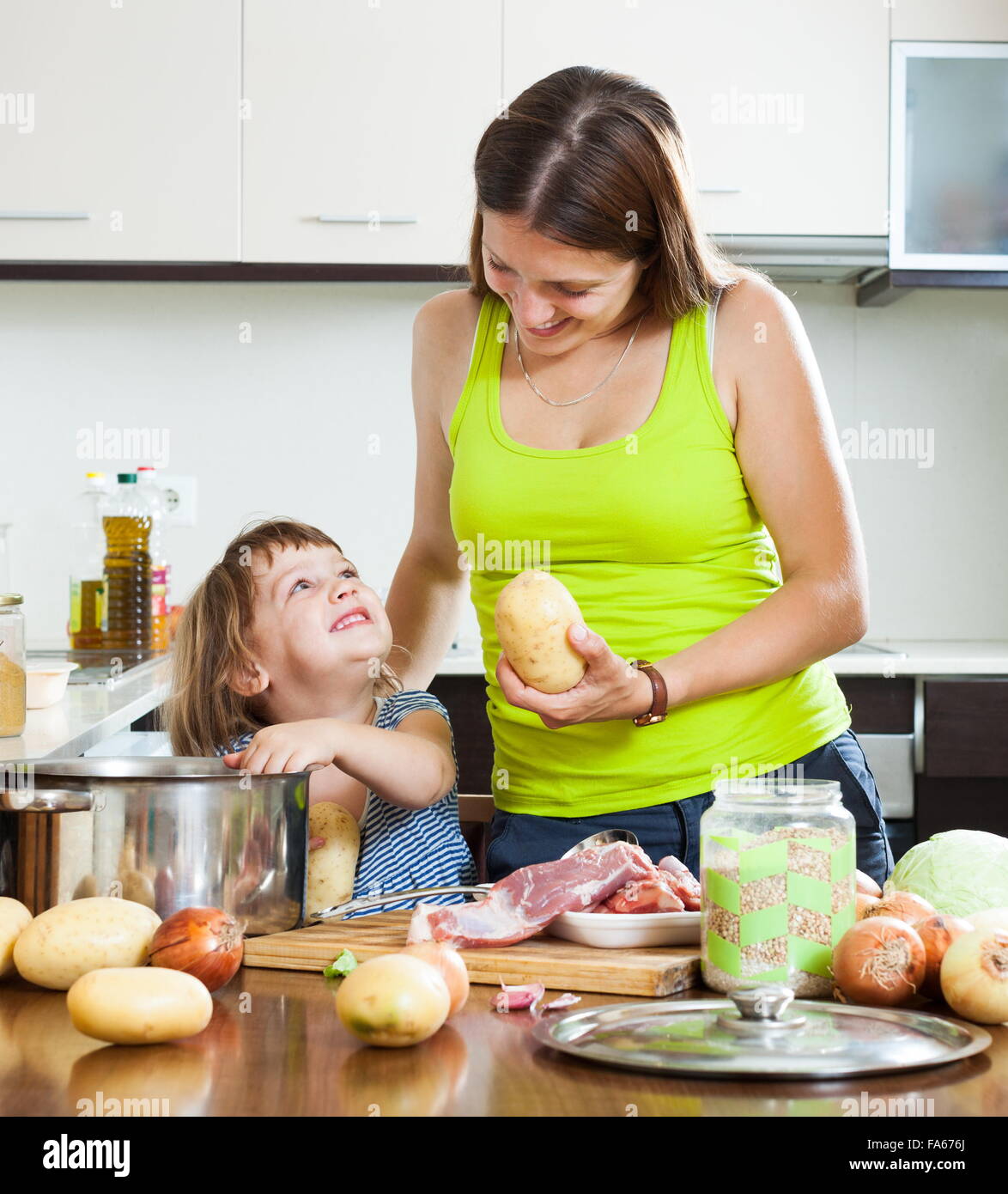 Smiling mother with child cooking with meat and vegetables Stock Photo ...