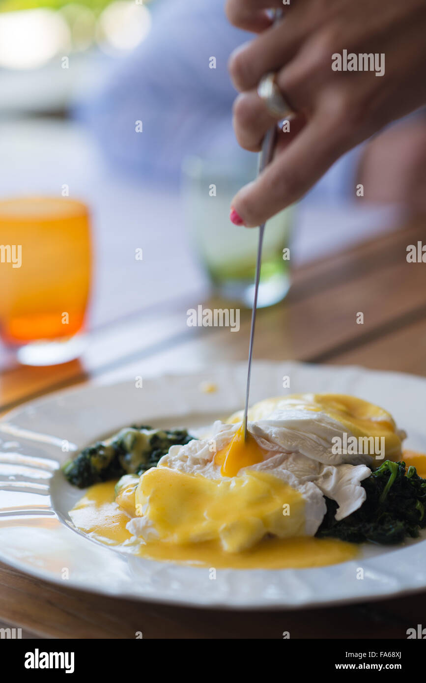 Human hand cutting into plate of eggs florentine Stock Photo - Alamy