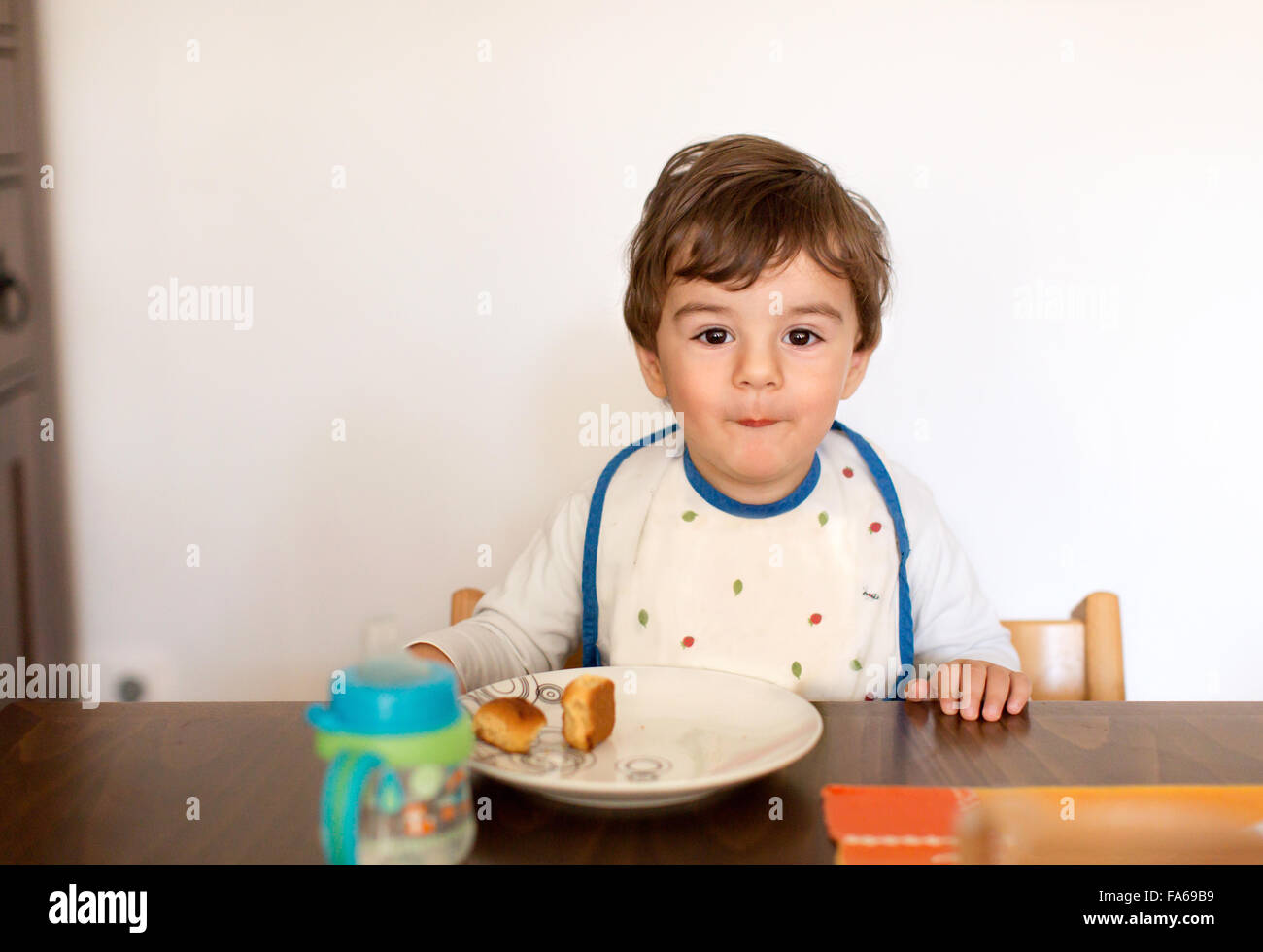 cheeky boy sitting at table eating snack Stock Photo - Alamy