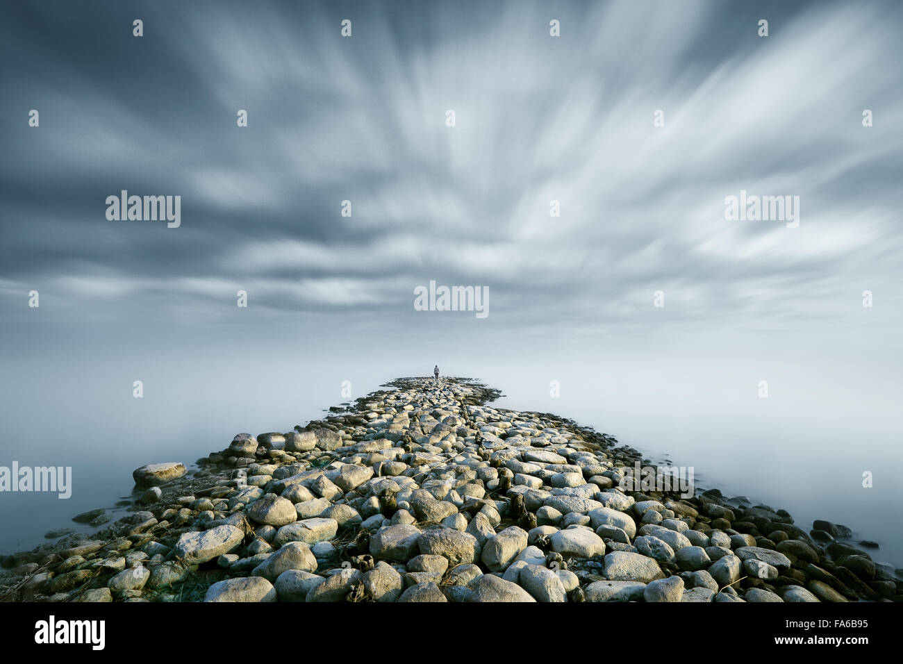 Woman standing in the distance at the end of a rocky coastal breakwater ...