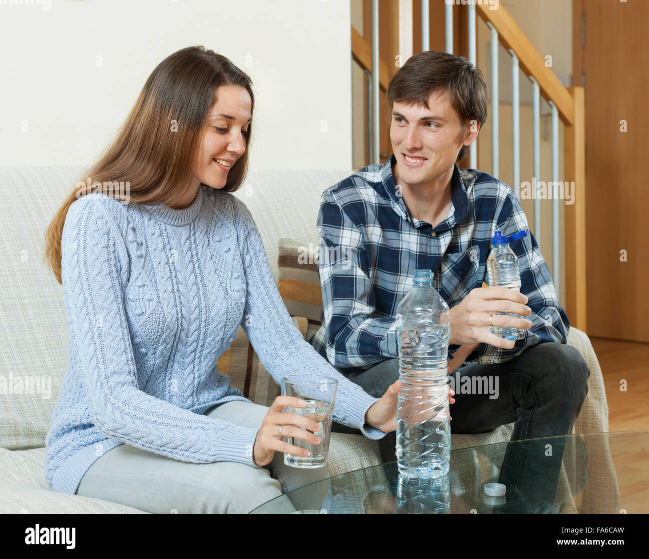 Happy couple drinking bottled water in home Stock Photo - Alamy