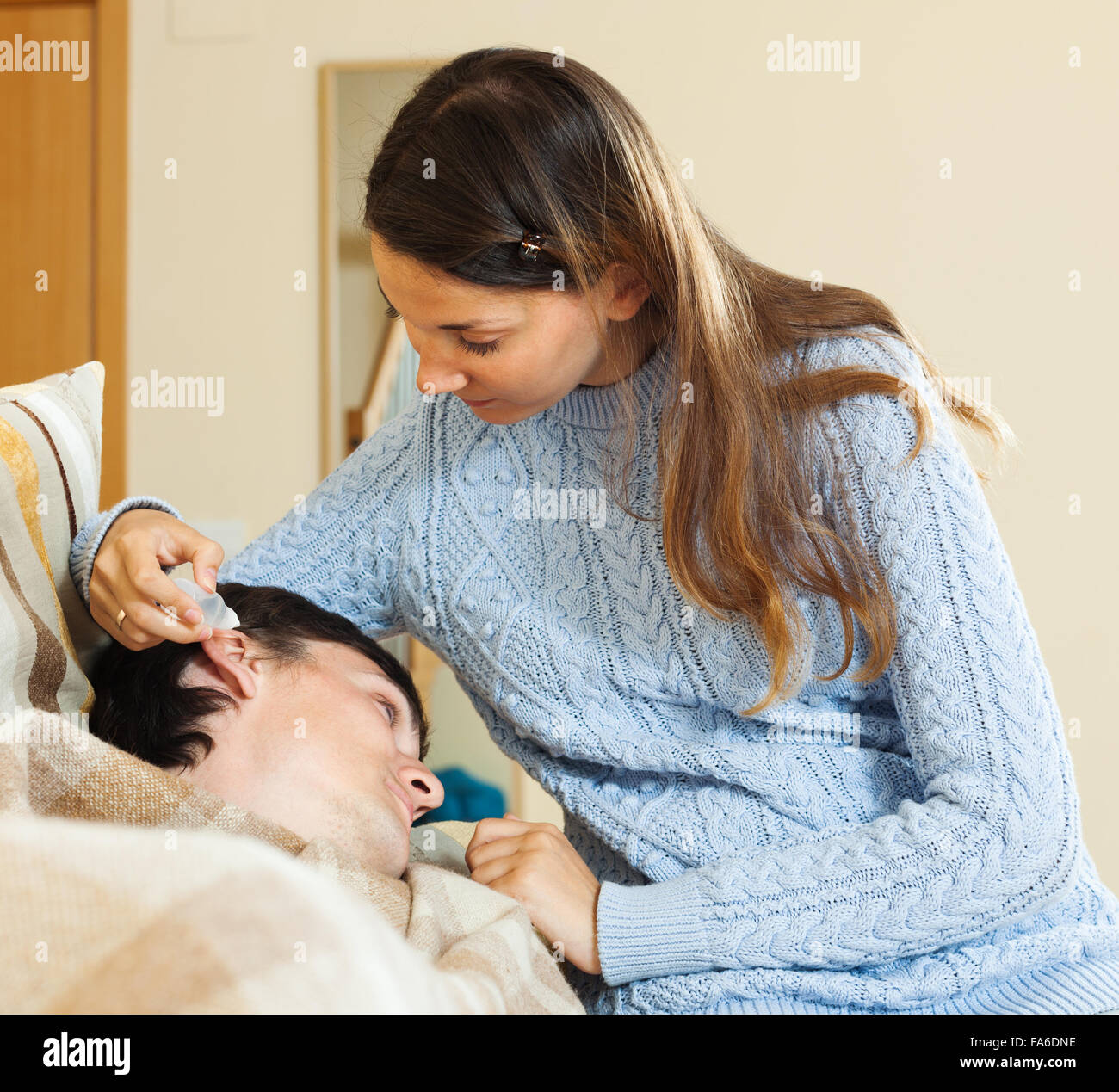 Young woman dripping ear drops to man in living room Stock Photo - Alamy
