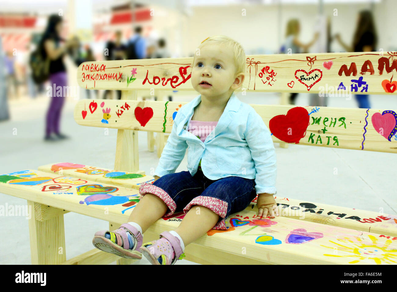 little fashionable baby sits on the bench with drawings and ...