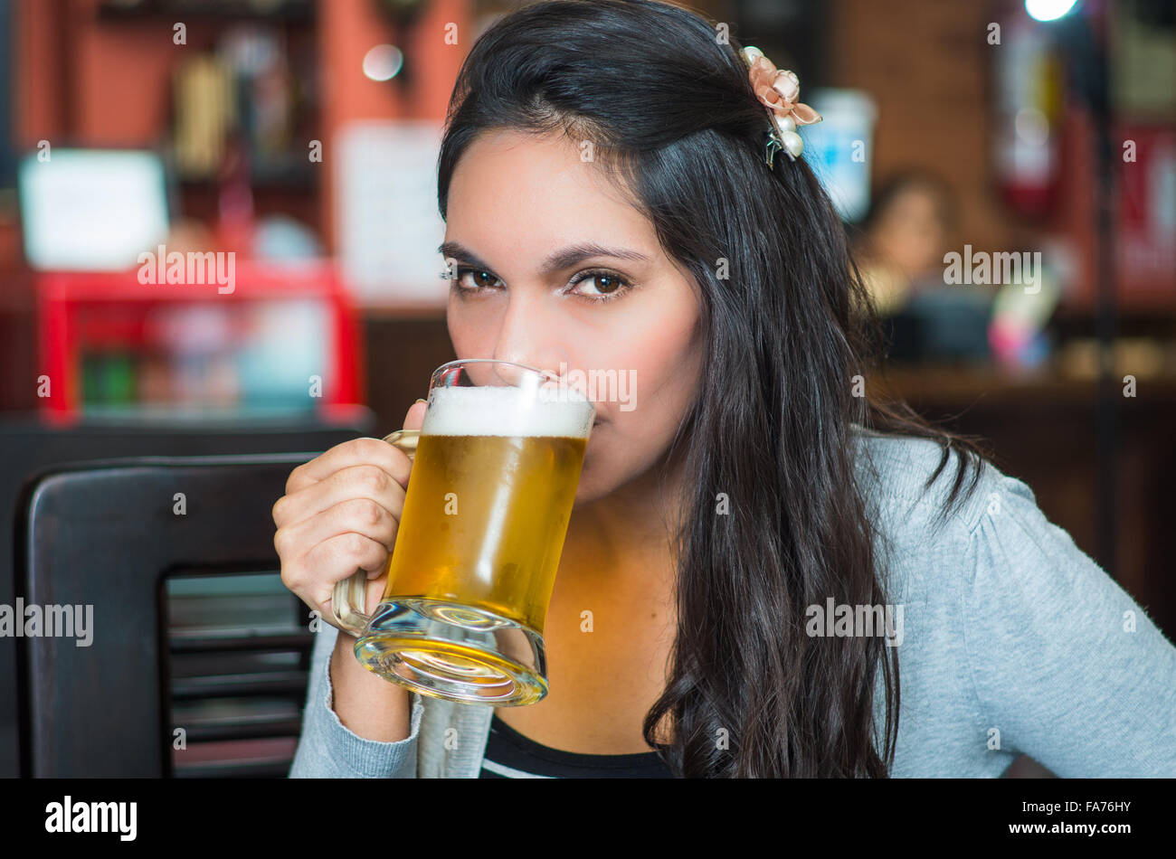 Brunette model sitting by restaurant table drinking from glass of beer ...