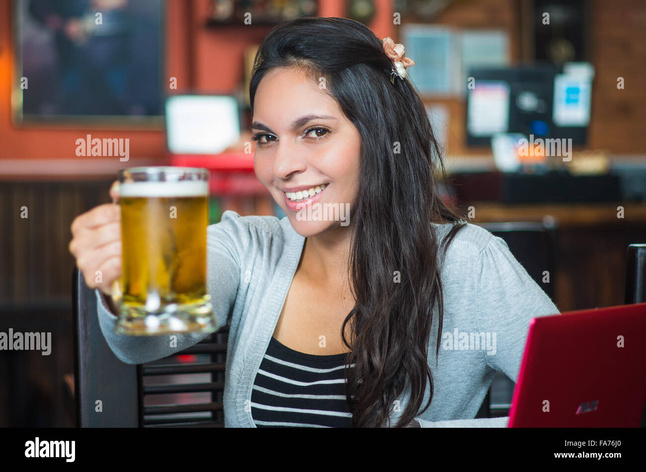 Brunette model sitting by restaurant table holding glass of beer and ...