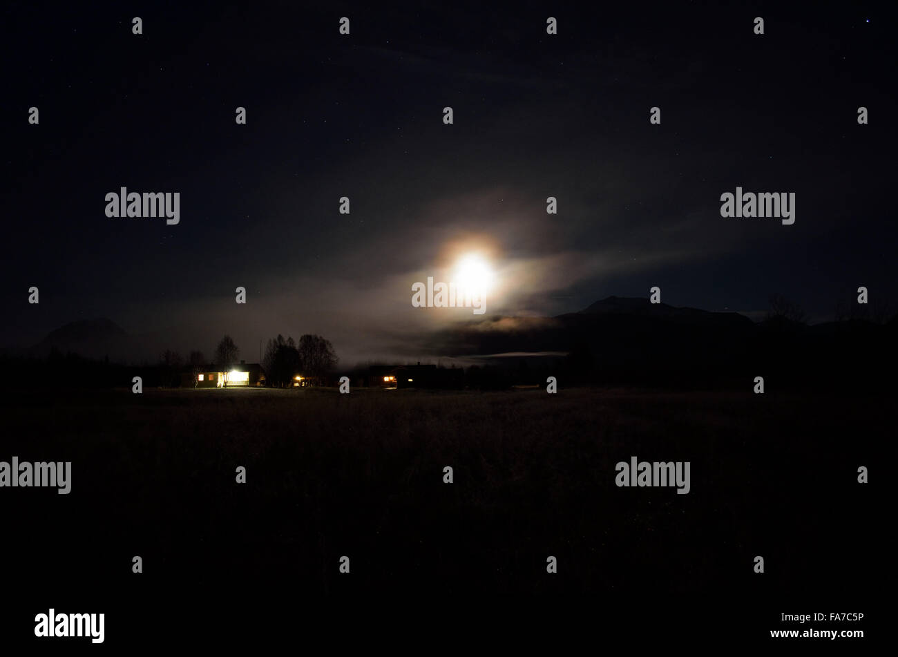 full moon on autumn night sky over mountain, field and lit houses Stock ...