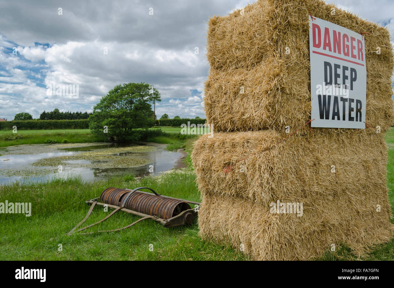Stack of hay bales with a warning sign next to deep water on a farm ...