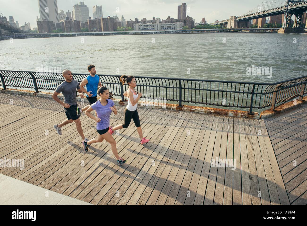 Four adult runners running along riverside, Brooklyn, New York, USA ...