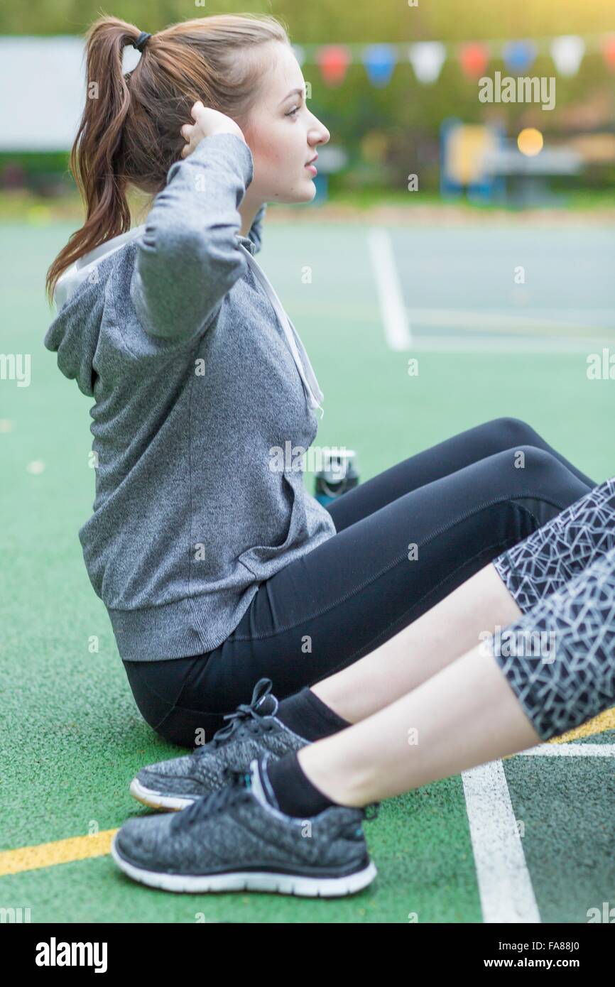 Side view of young woman on sports court, hands behind head doing sit ...