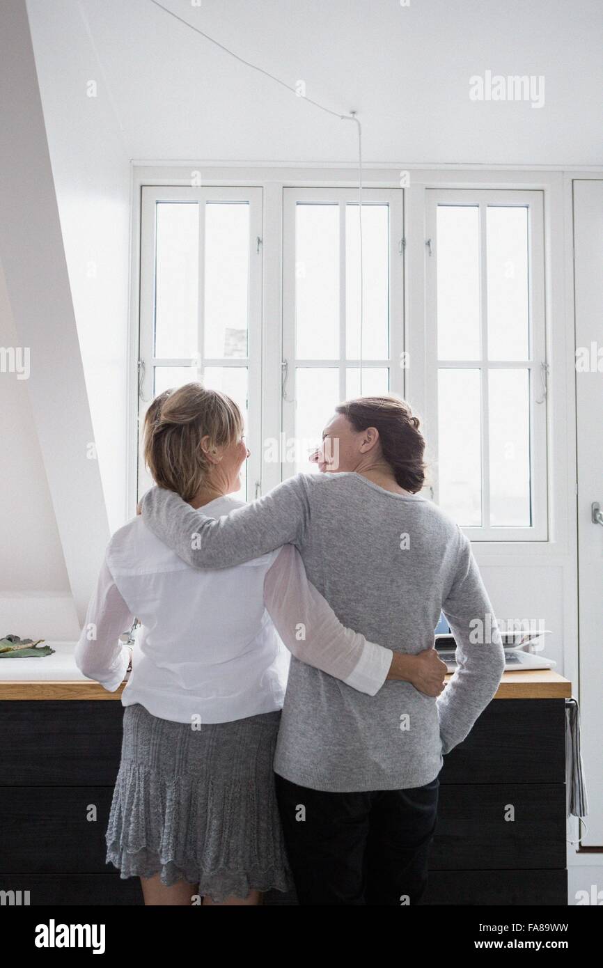 Two mature women, standing in kitchen, hugging, rear view Stock Photo ...