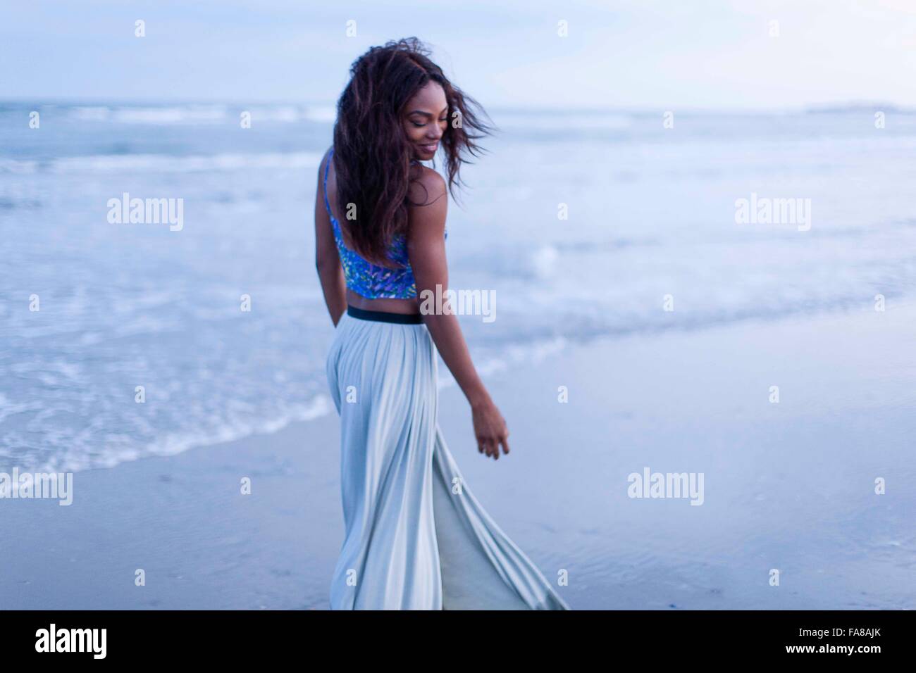 Young woman walking on beach, looking over shoulder, smiling Stock ...