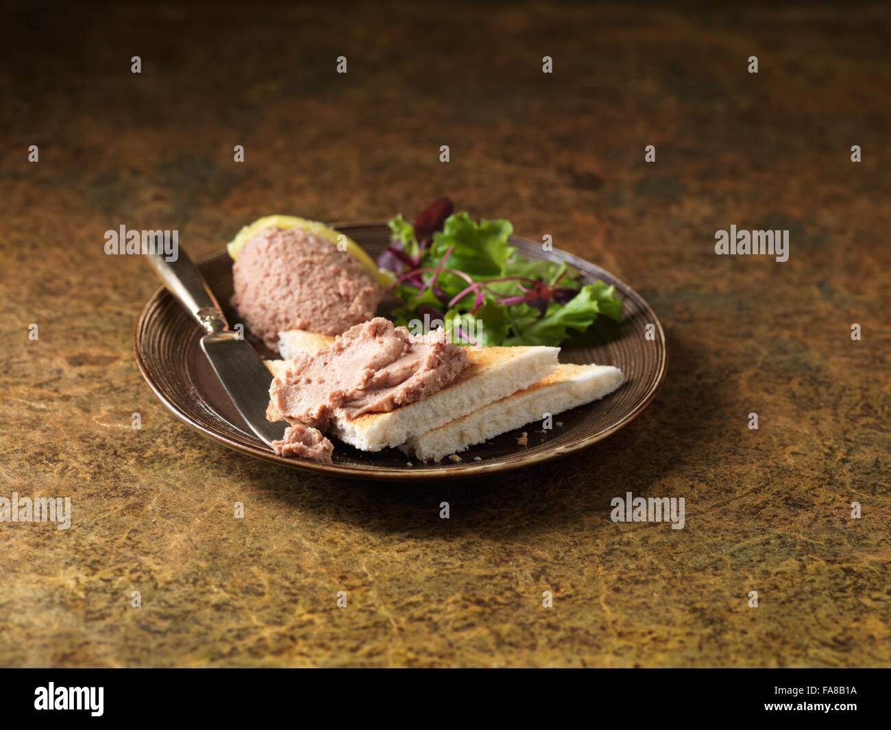 Duck parfait smeared on triangular toast with salas and knife on brown ...