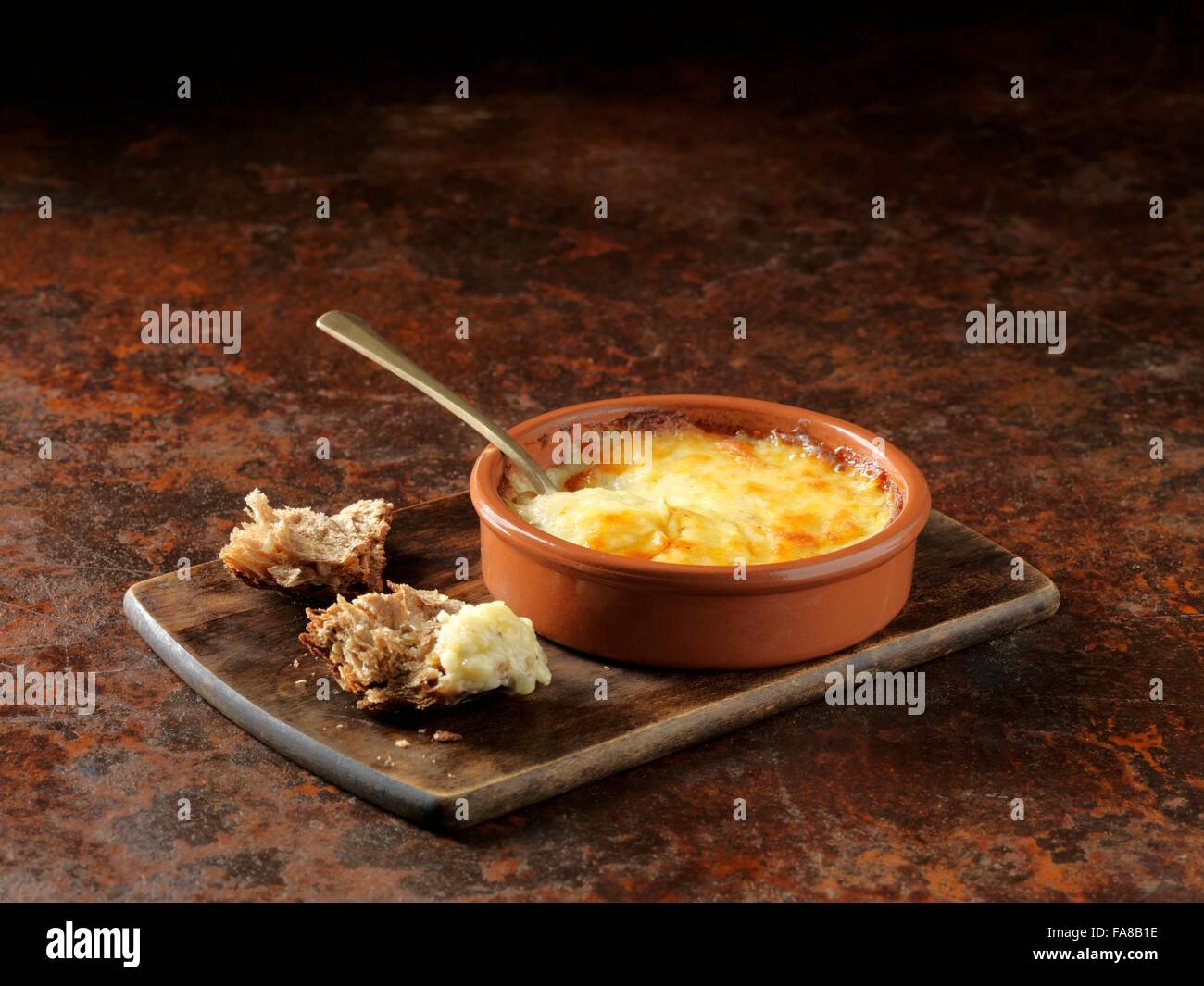 Emmental, Gruyer and Calvados cheese baked in terracotta dish and torn ...