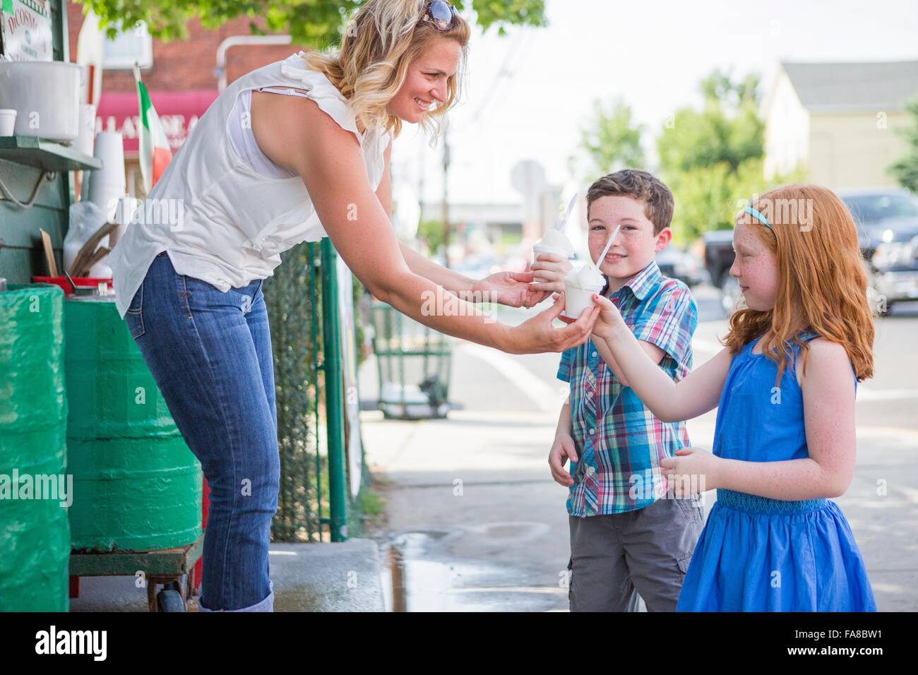Ice cream parlour shop keeper handing ice cream to brother and sister ...