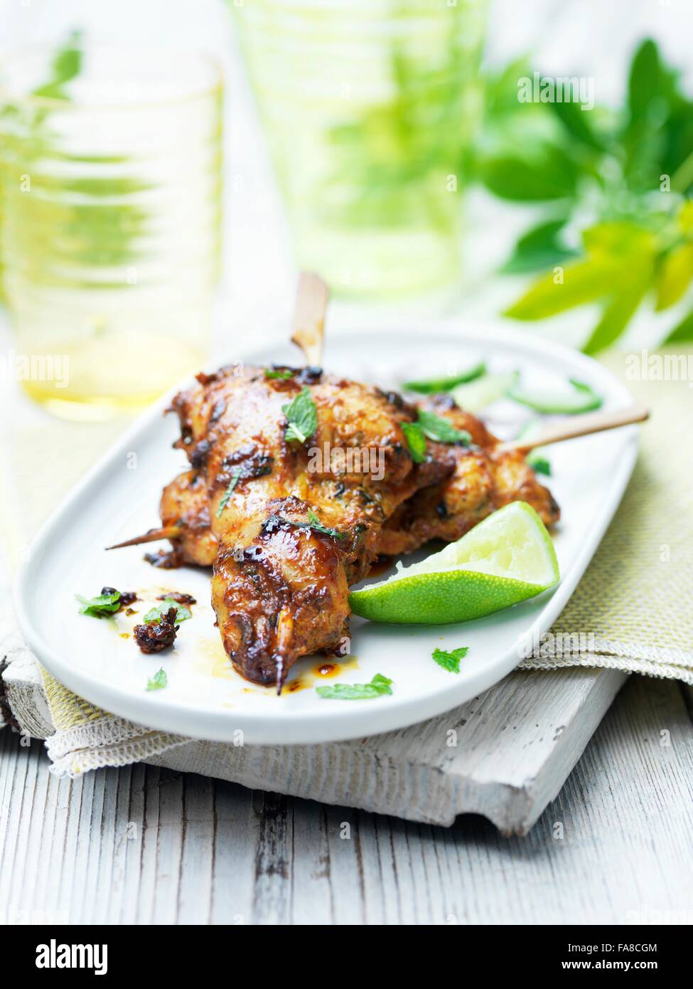 Dish of chicken tikka kebabs, lime slice on wooden table in garden ...