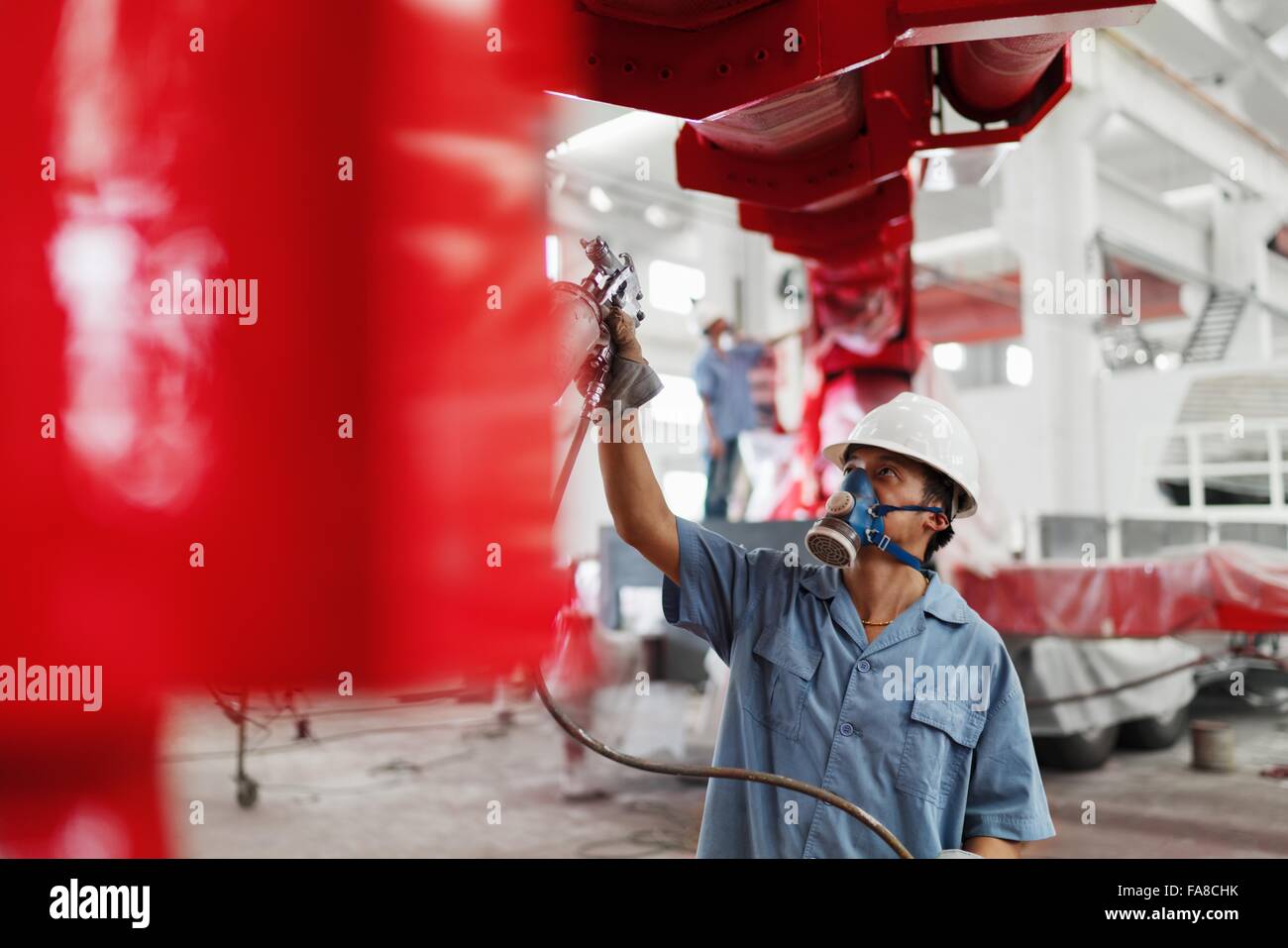 Male factory worker spray painting a red crane in factory workshop ...