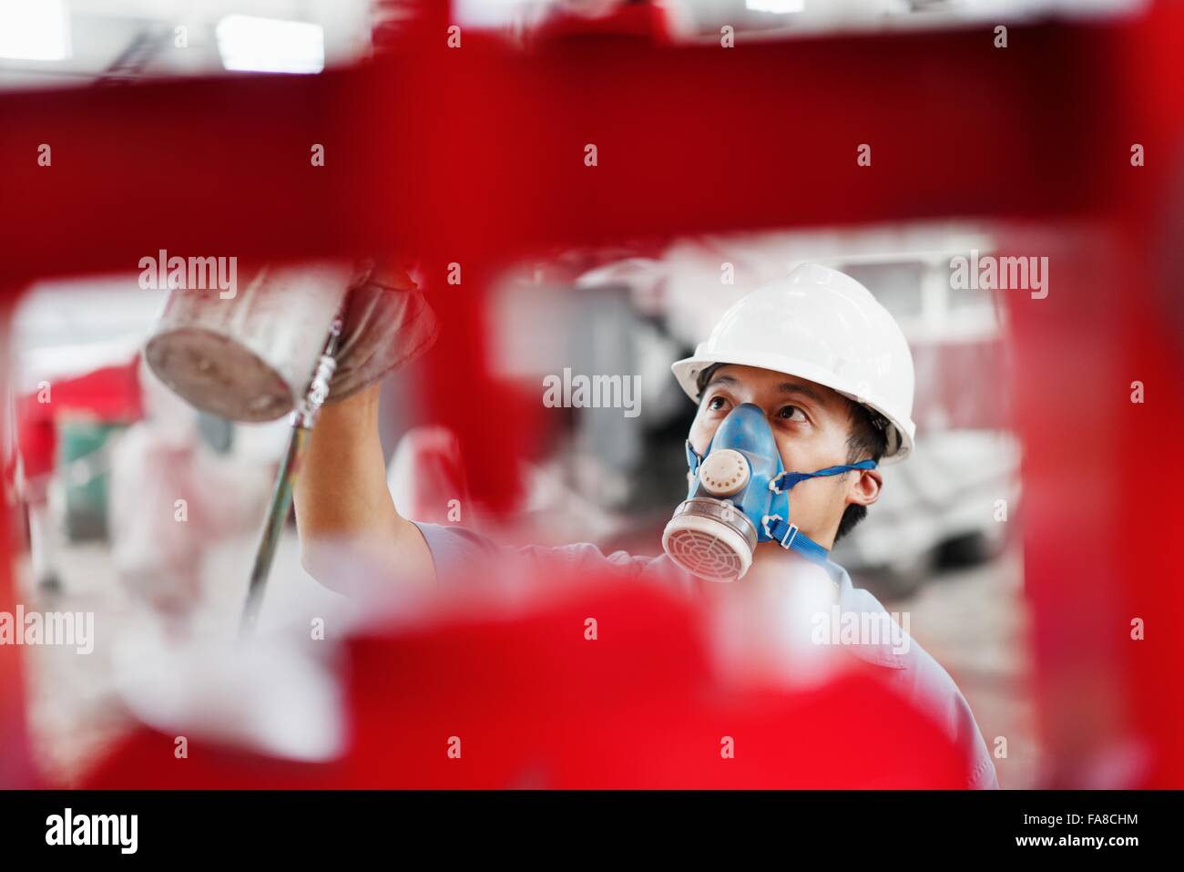 Close up of male factory worker spray painting a red crane in factory ...
