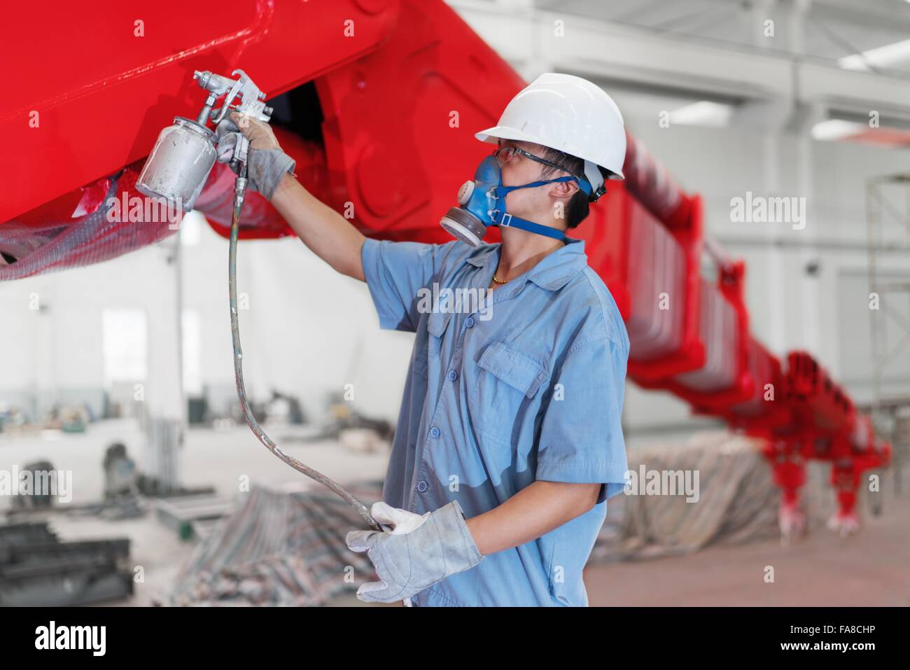 Male worker spray painting a crane arm red in factory workshop, China ...